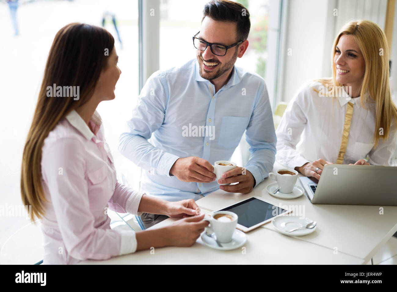 Cheerful workteam in office working together on laptop and drinking ...