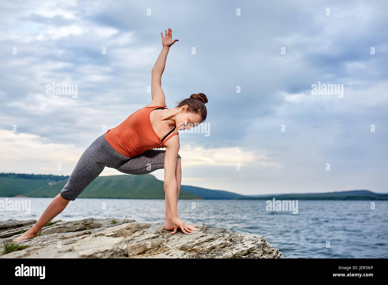 Young woman standing in yoga pose on the big stone near beautiful river ...