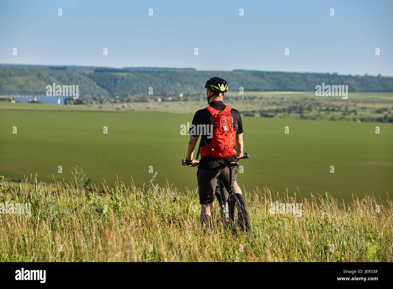 Rear view of the cyclist standing of the hill against beautiful summer ...