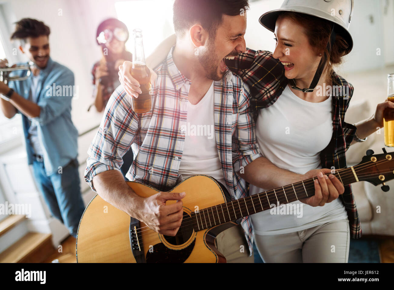 Cheerful young friends having party together and playing instruments ...