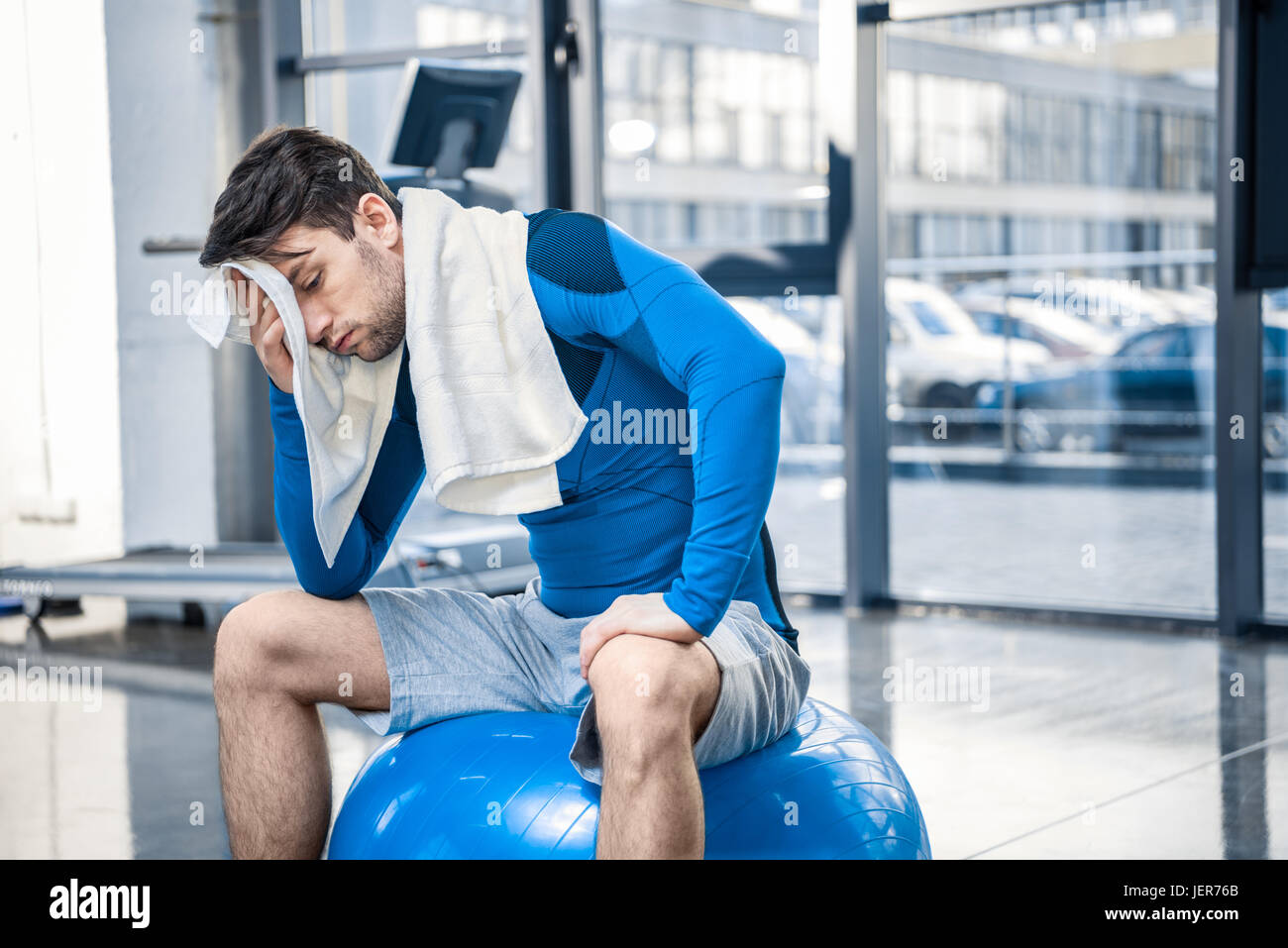 Tired young man resting on fitness ball at gym Stock Photo - Alamy