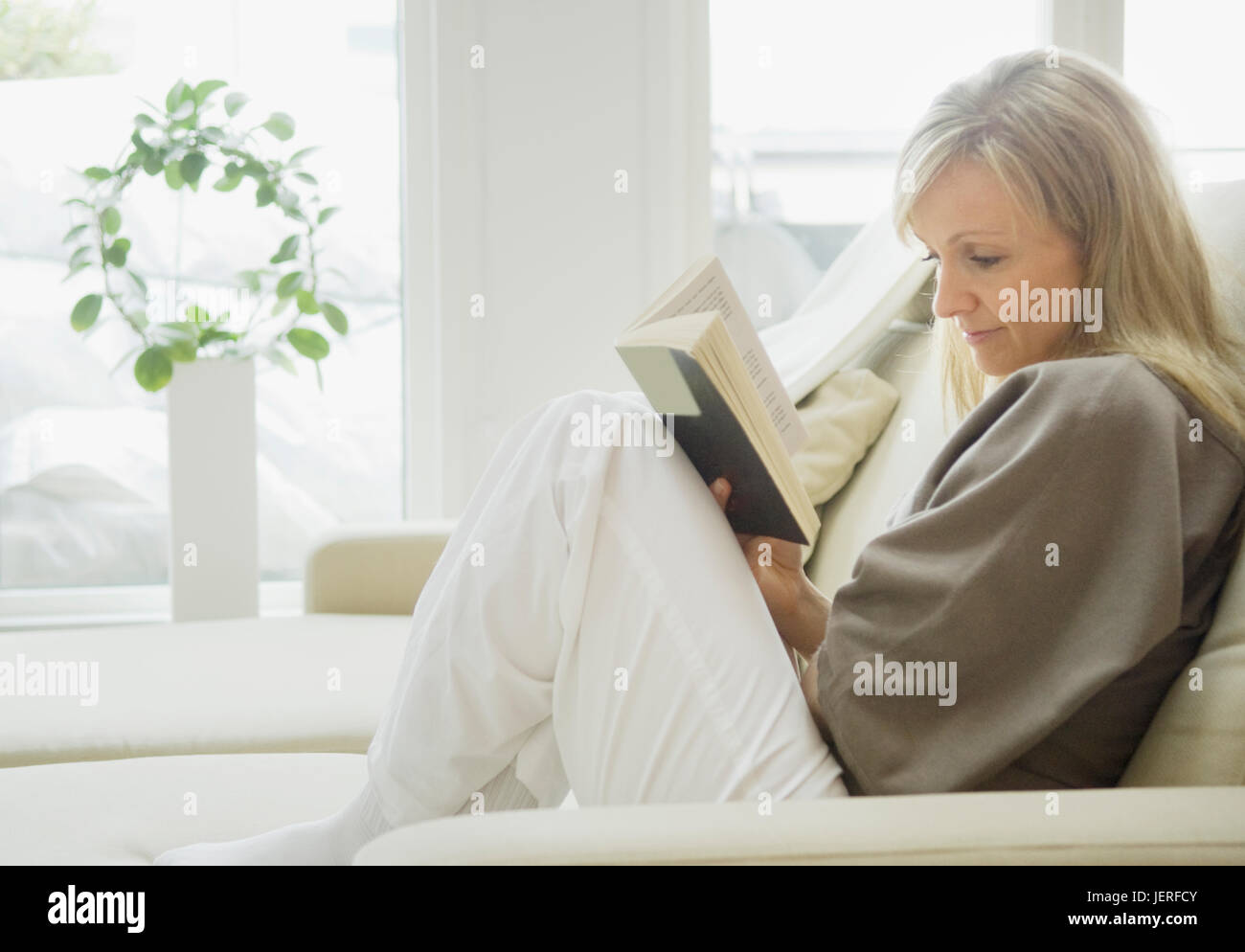 Woman reading book on sofa Stock Photo - Alamy