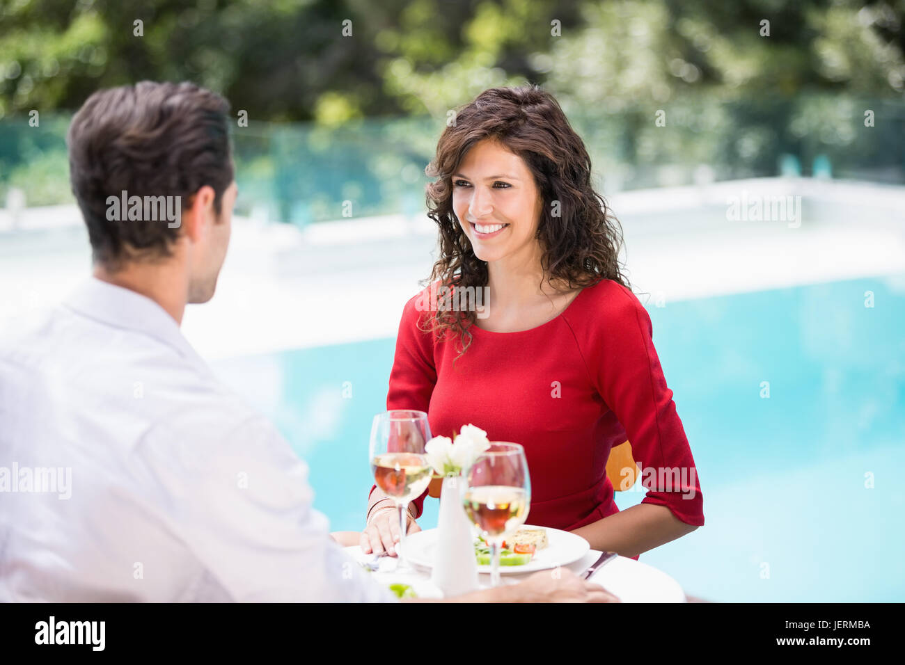 Smiling couple sitting by swimming pool Stock Photo - Alamy