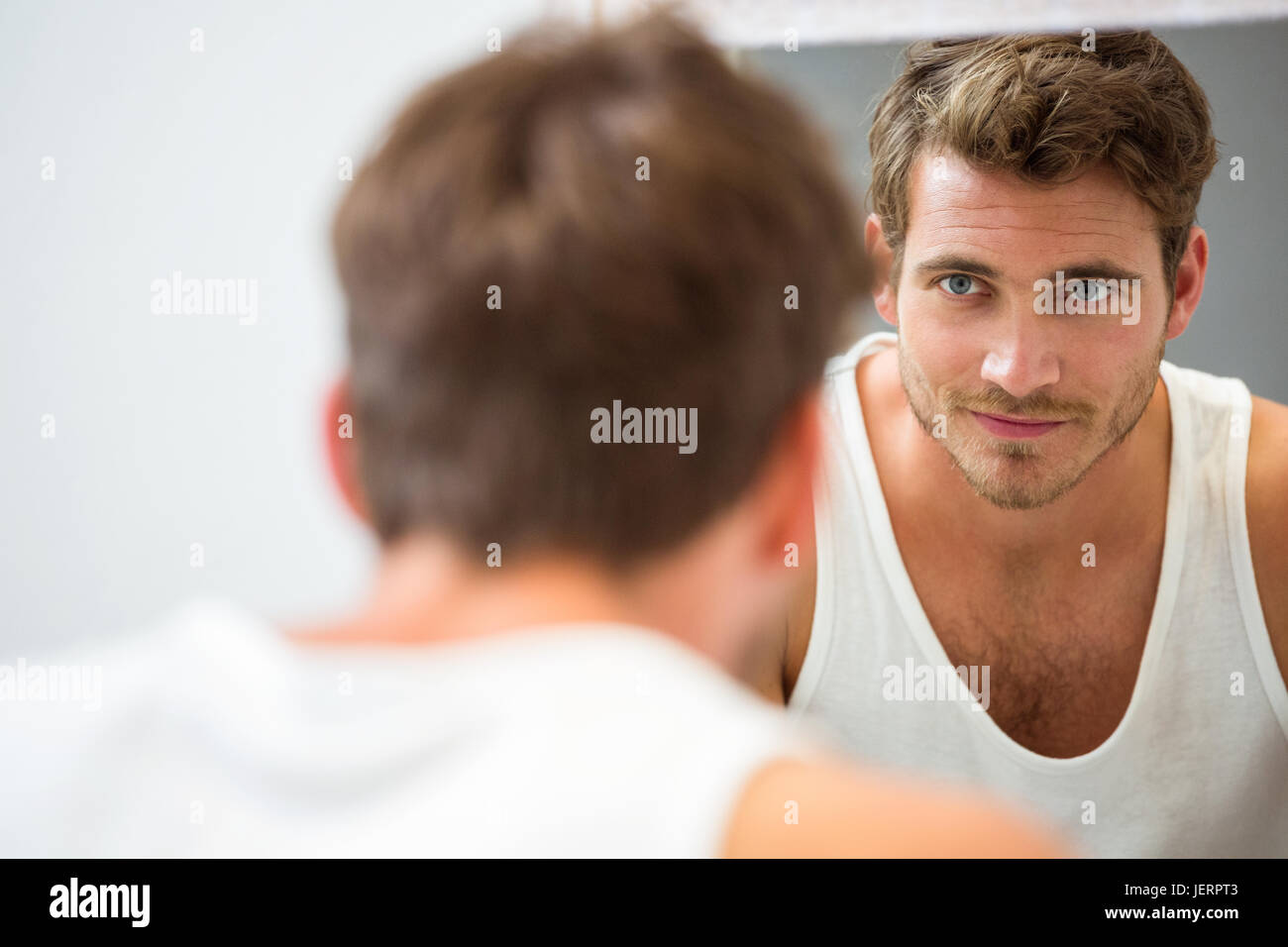 Young man looking at himself in mirror Stock Photo - Alamy