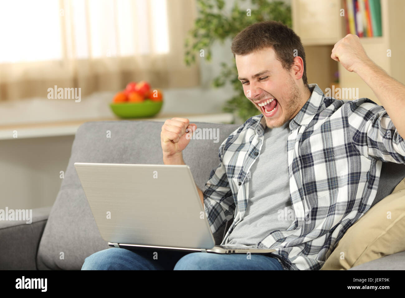 Excited man on line with a laptop sitting on a couch in the living room ...