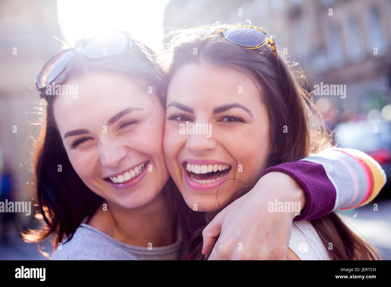 Two friends hugging in the city. They are looking at the camera and ...