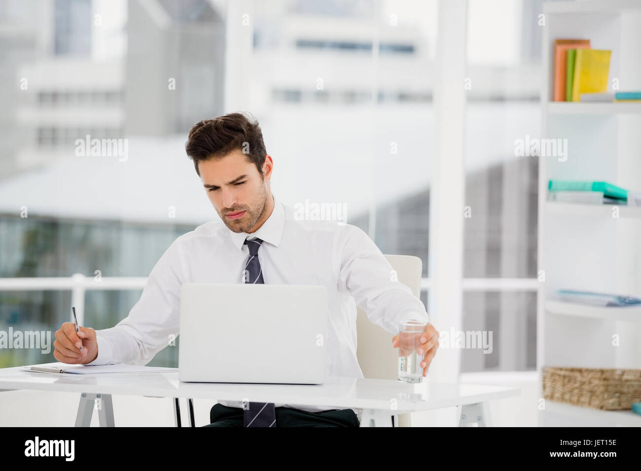 Businessman using laptop and taking notes Stock Photo - Alamy