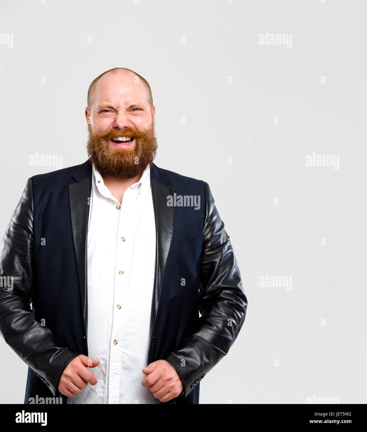 Laughing man with ginger beard in black jacket on empty gray background ...