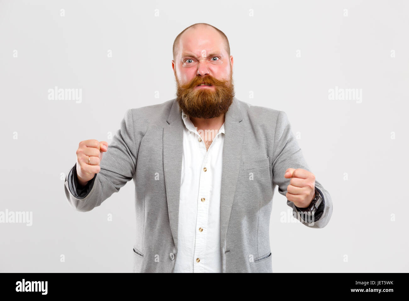 Angry man with ginger beard clenching his fists on gray empty ...