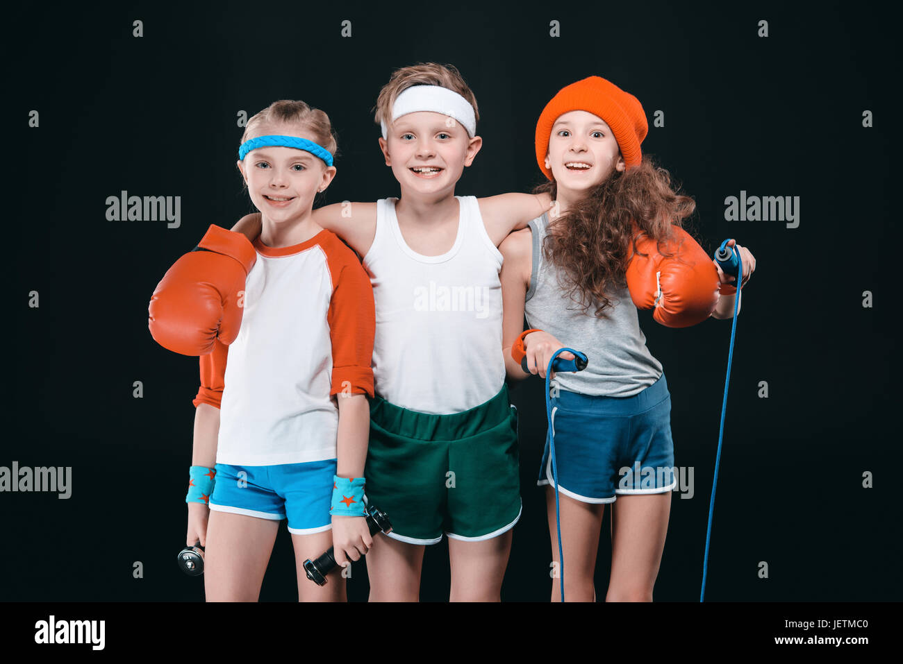 Three smiling kids in sportswear posing with sport equipment and ...
