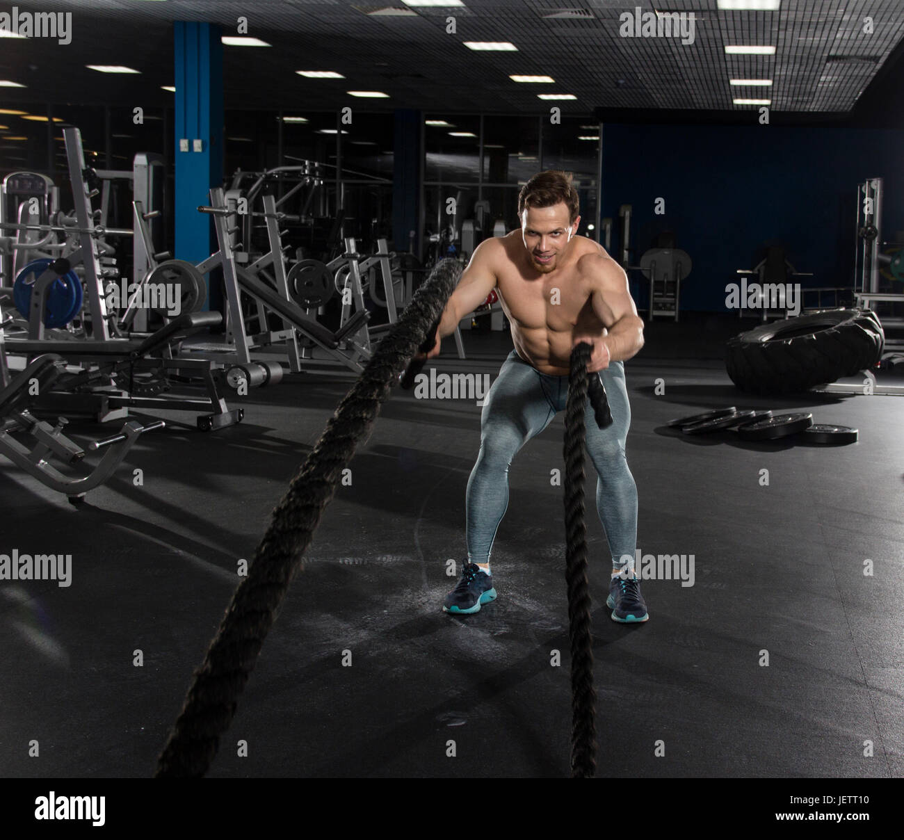 Muscular athlete with battle ropes exercise in modern fitness center ...