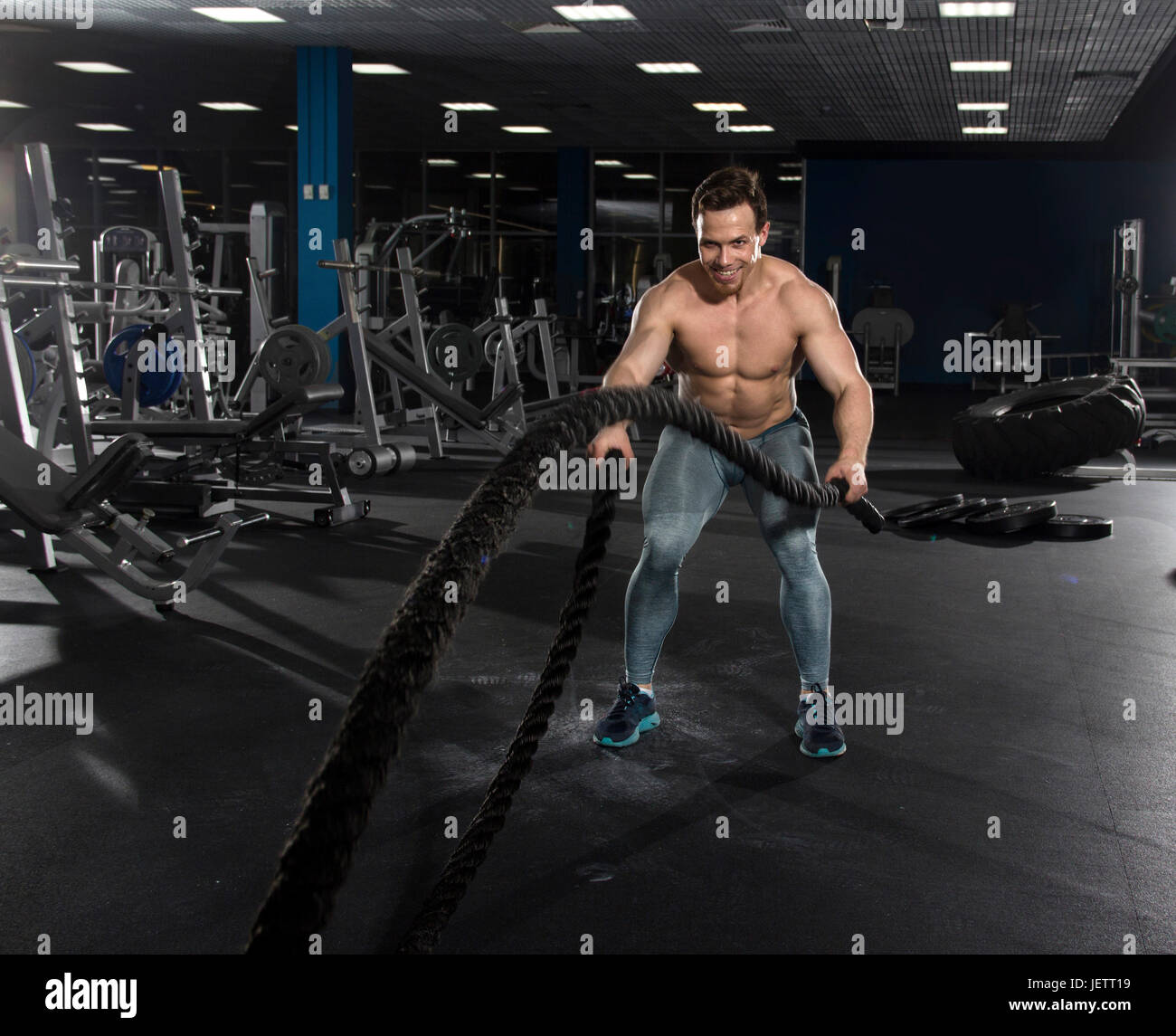 Muscular athlete with battle ropes exercise in modern fitness center ...