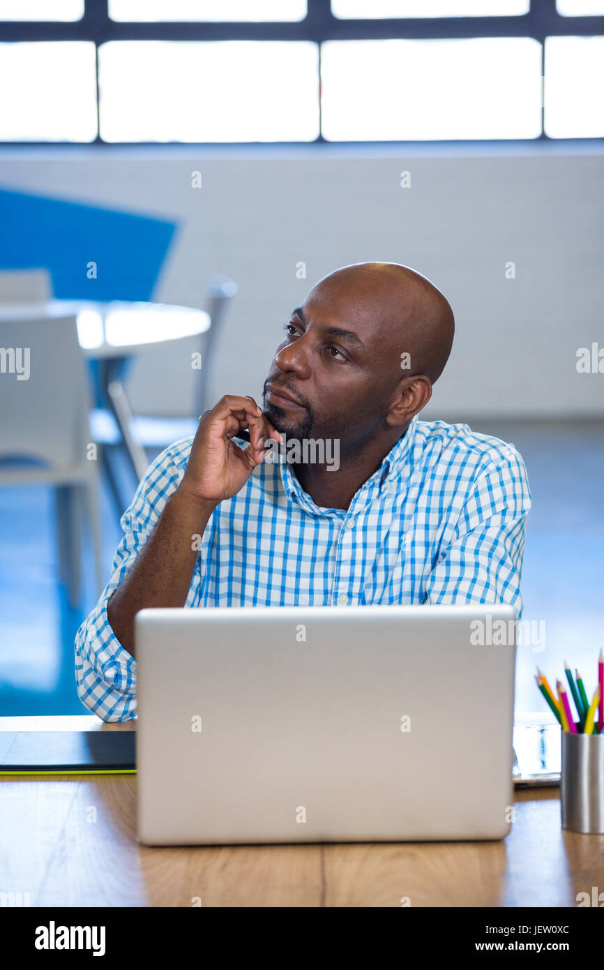 Thoughtful man sitting on table with laptop Stock Photo - Alamy