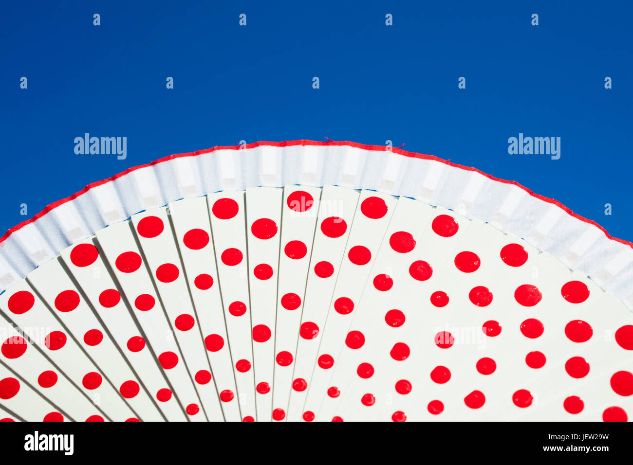 White Hand-held fan (or spanish fan) with red dots and blue sky in ...
