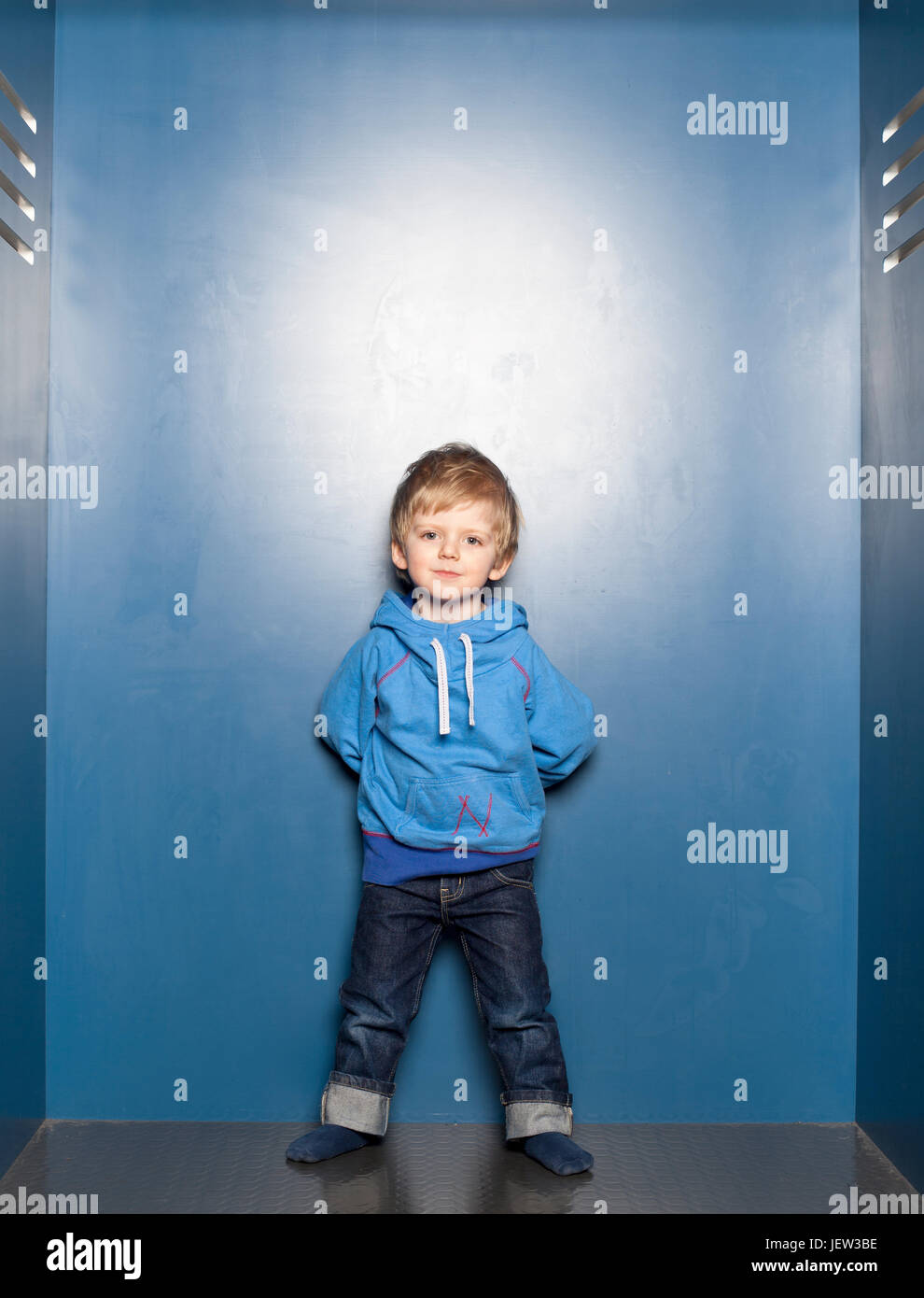 Boy standing against blue wall Stock Photo - Alamy