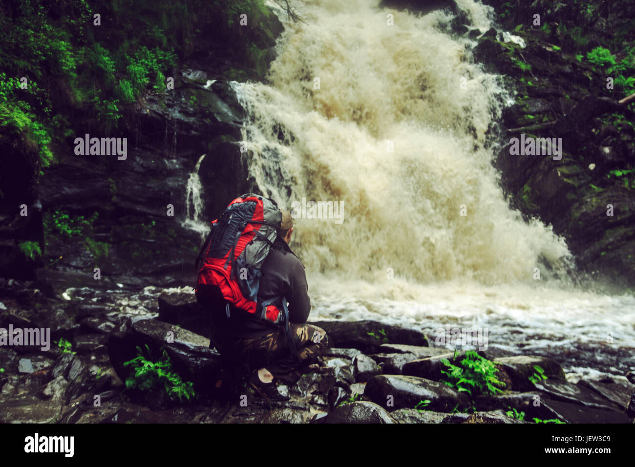 Traveler with a backpack near waterfall. It's raining Stock Photo - Alamy