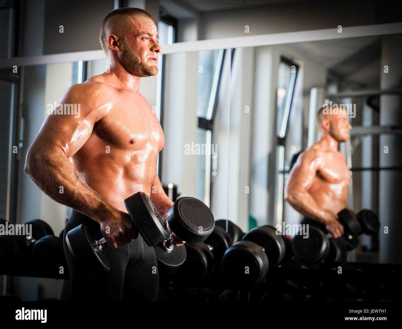 Muscular, strong man working out with dumbbells next to a mirror. Arm ...