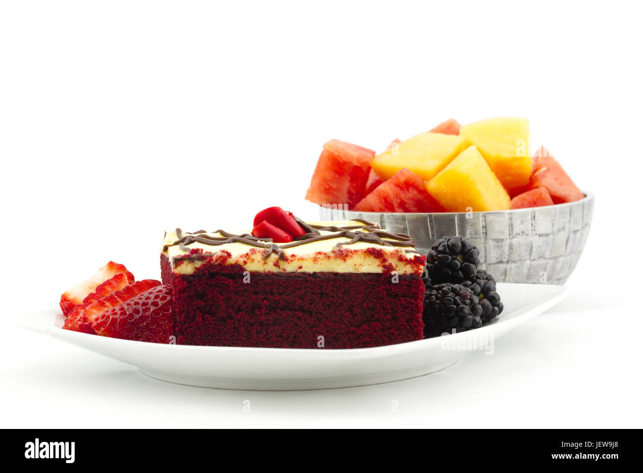 Square cut of iced red velvet cake with berries and metal bowl filled ...
