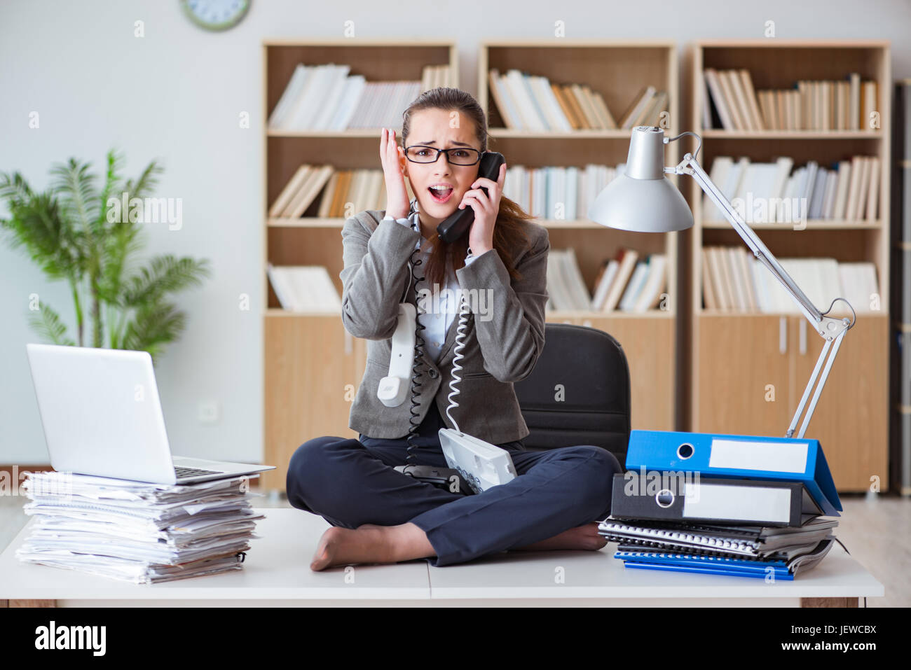 Busy angry businesswoman sitting on the desk in office Stock Photo - Alamy