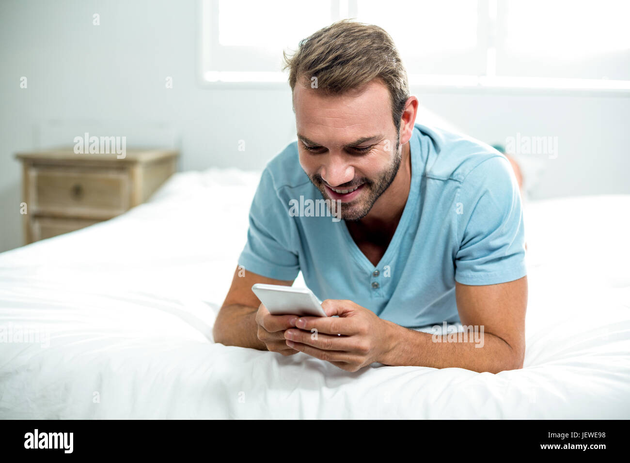 Happy man using cellphone on bed Stock Photo - Alamy