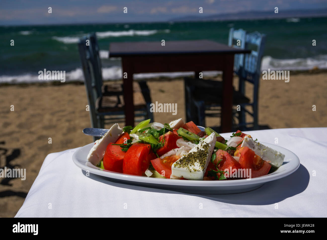 Xoriatiki salad served on a table by Greek beach with blurred beach ...