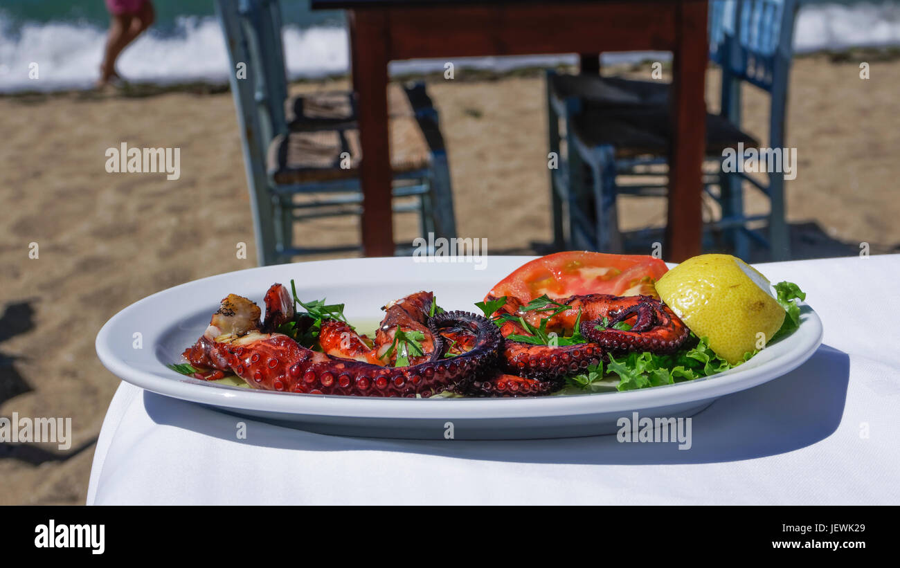 Grilled octopus legs served on a table by Greek beach with blurred ...