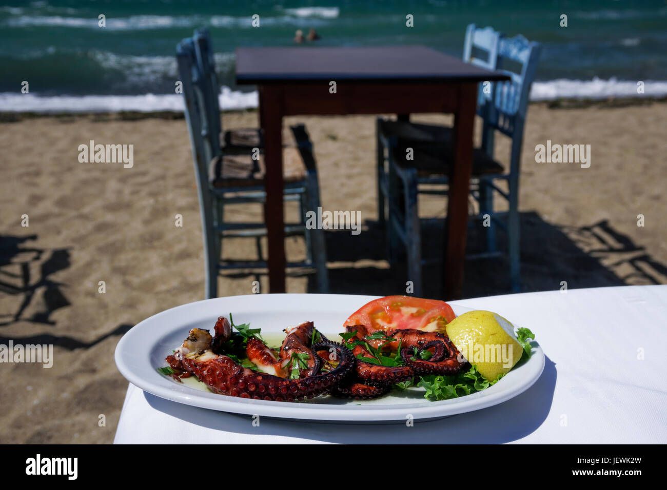 Grilled octopus legs served on a table by Greek beach with blurred ...