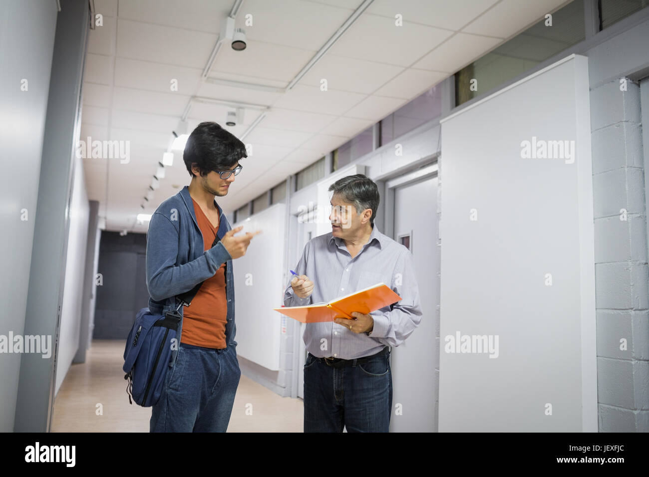 Professor with notebook talking to a student Stock Photo - Alamy