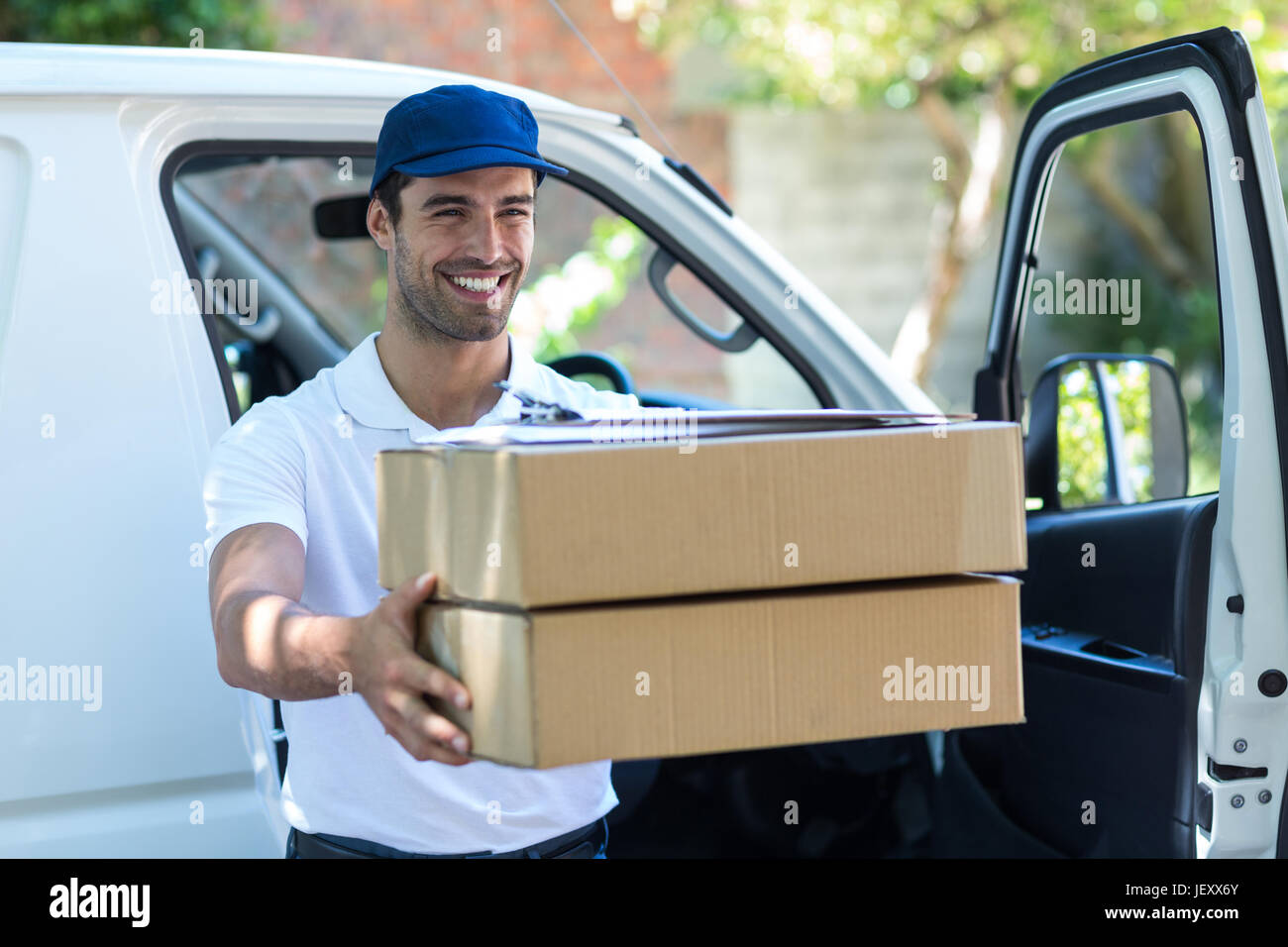 Smiling delivery man giving cardboard boxes Stock Photo - Alamy