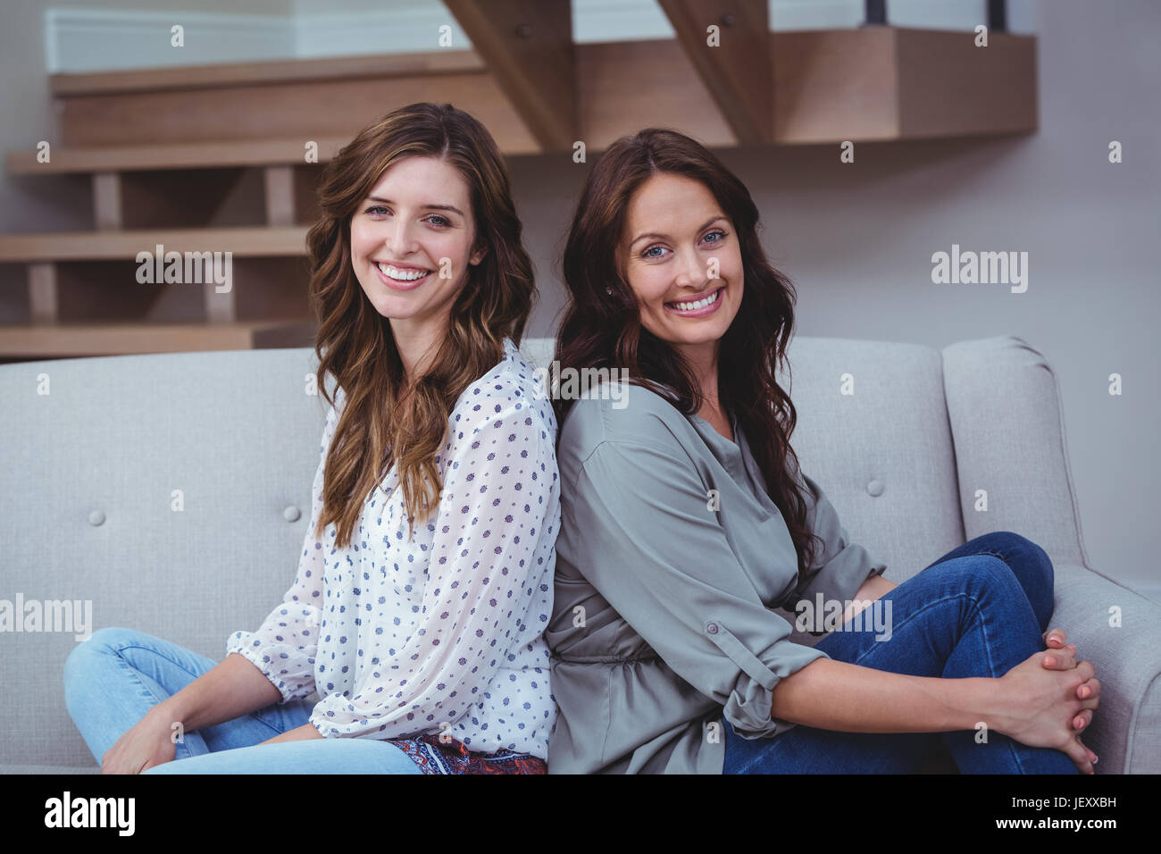 Two beautiful sitting back to back on sofa Stock Photo - Alamy