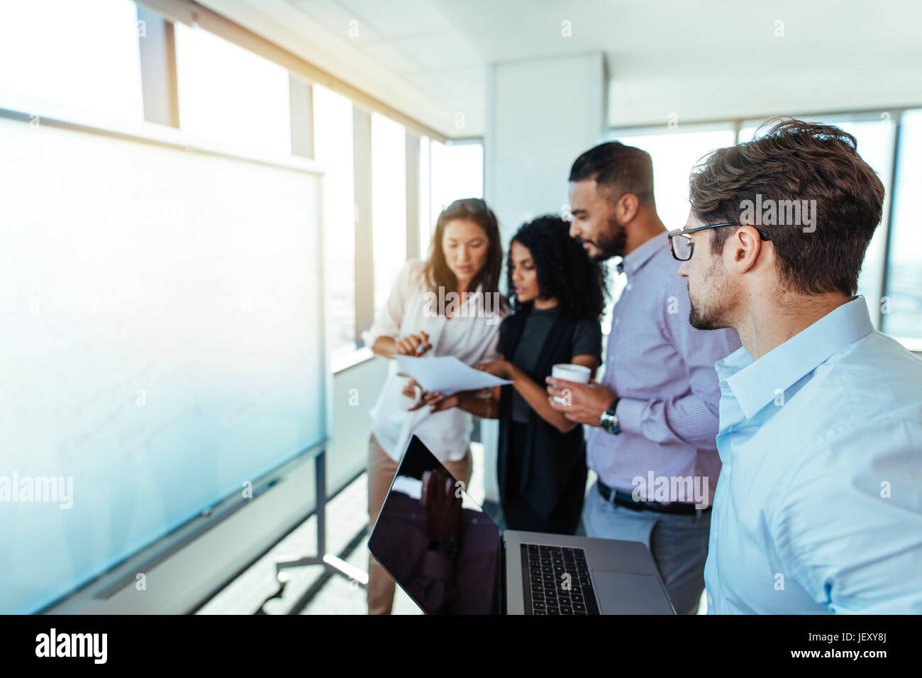 businesswomen discussing a point on paper while a man works on computer ...