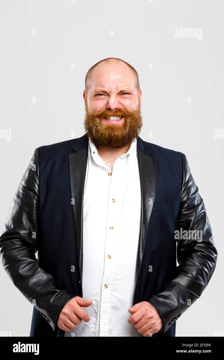 Happy man with ginger beard in black jacket on empty gray background ...