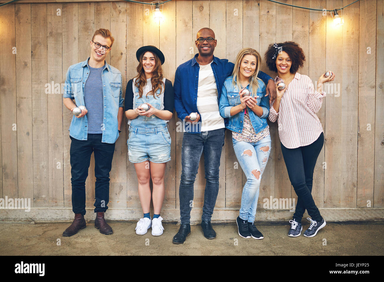 Cheerful black and white group of friends standing at wooden wall and ...