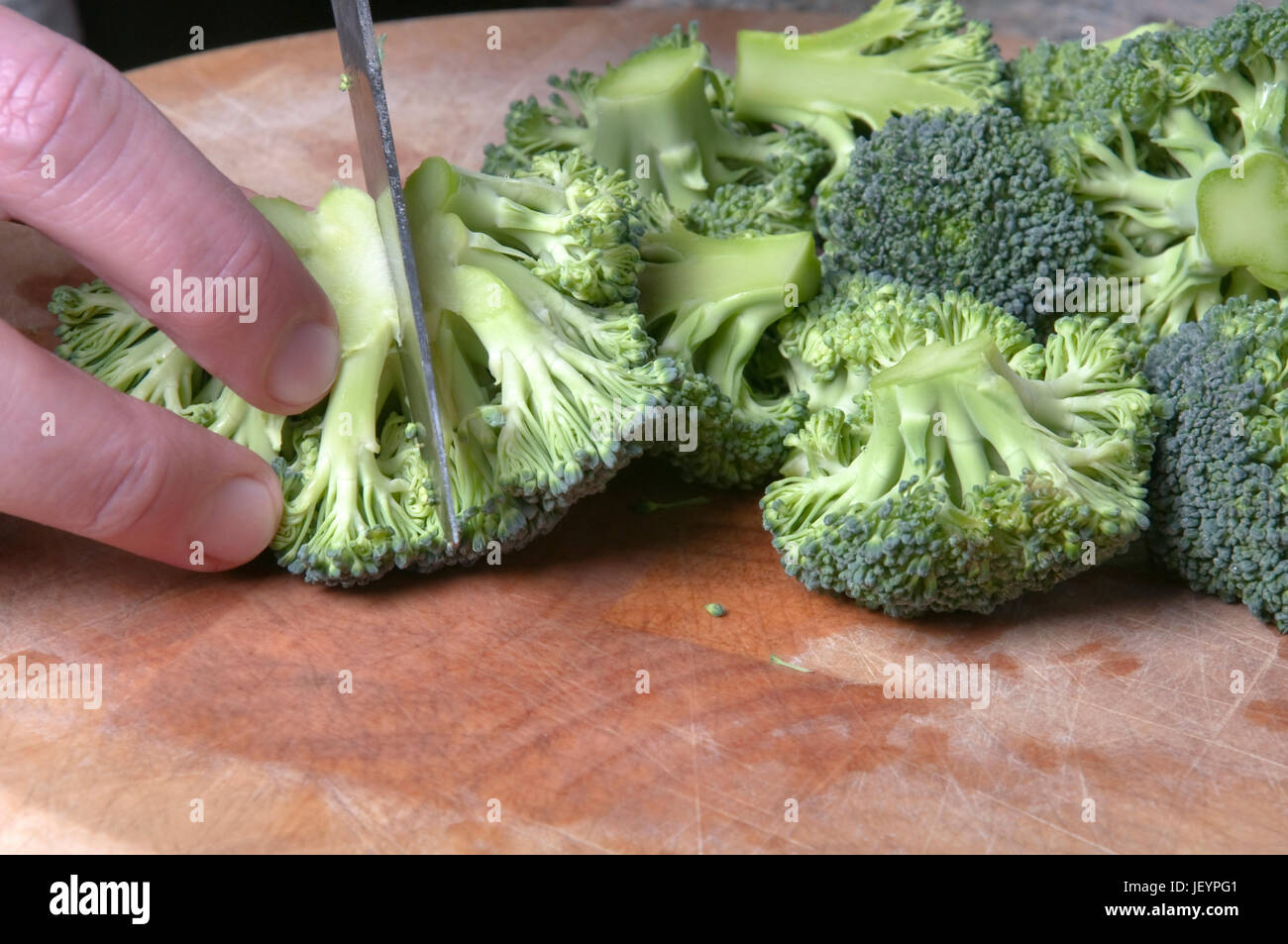 Close up of a man's hand chopping washed broccoli with a steel knife on ...