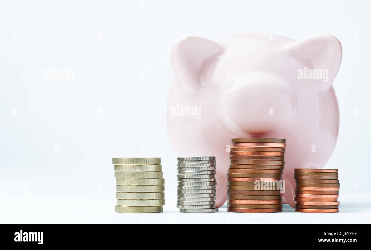 A pink piggy bank, facing front and looking over some coin stacks. The ...