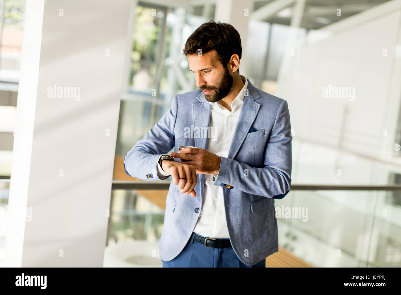 Handsome young business man is looking at his watch in modern office ...