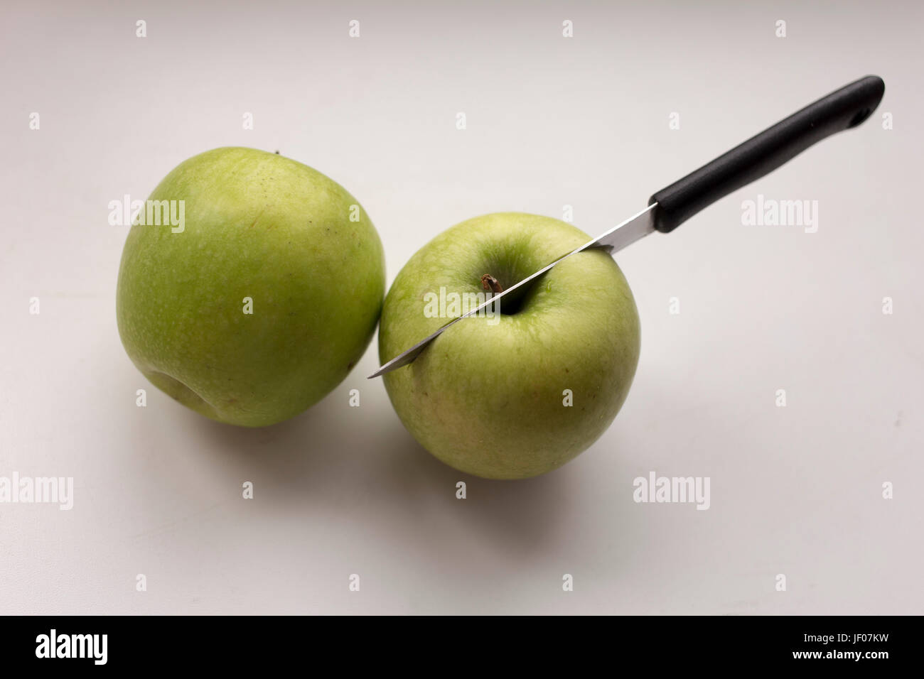 The knife pierced the apple. Two green apples on a white background ...