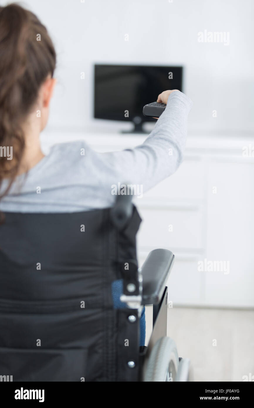 Rear view of lady in wheelchair changing tv channel with remote control ...