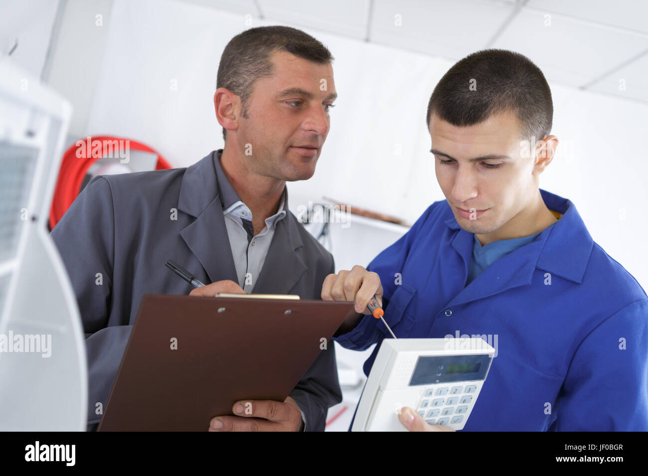 One man with clipboard, another using screwdriver Stock Photo - Alamy