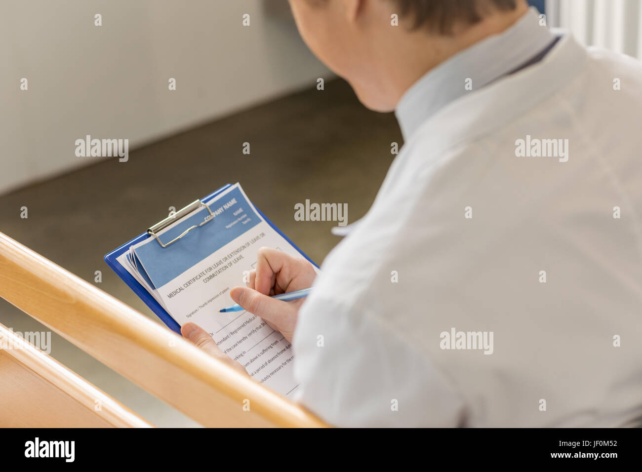 rear view of young doctor writing diagnosis on clipboard in hospital ...