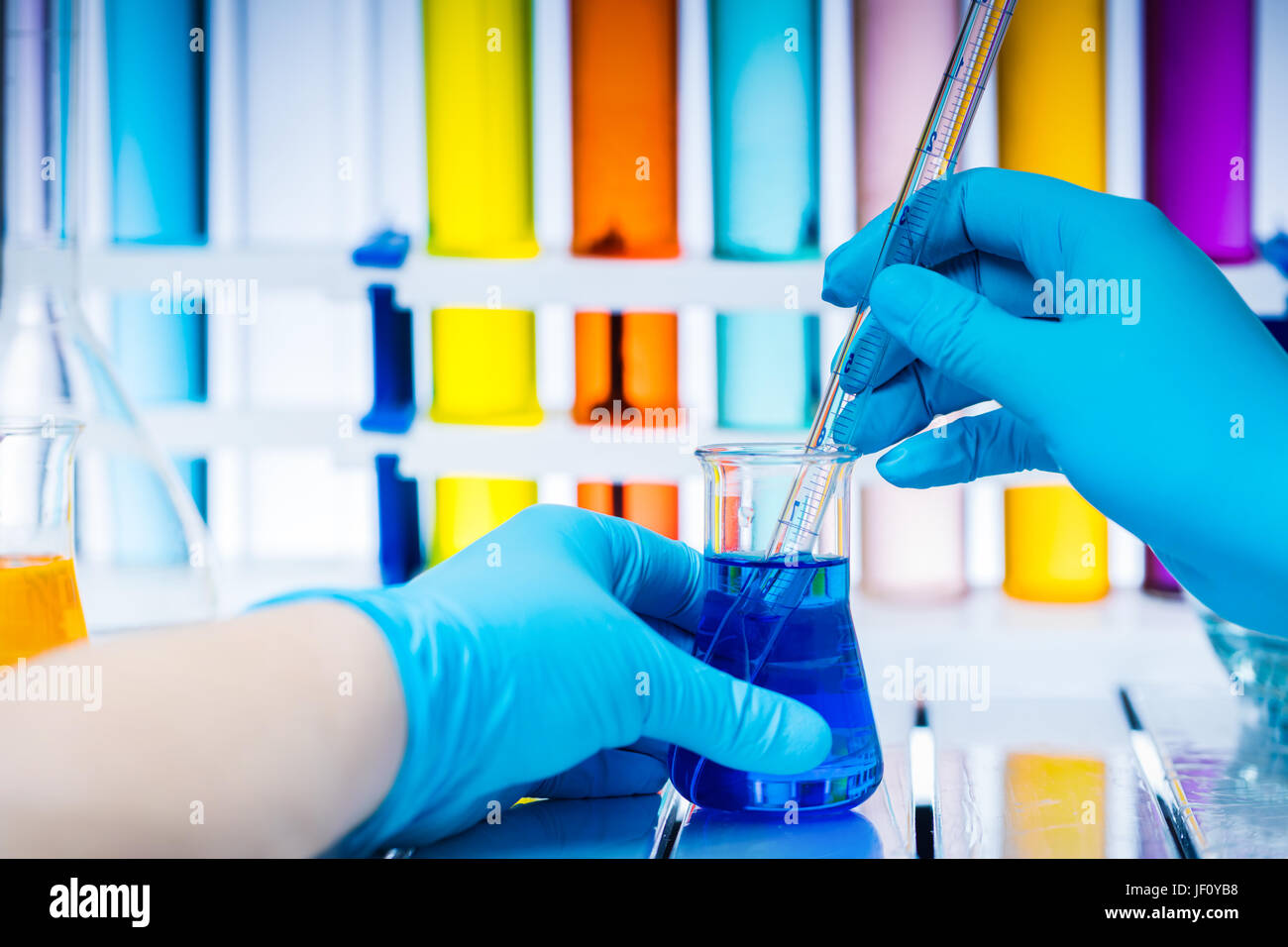 Laboratory worker holds a flask and a pipette, analyzes blue chemical ...