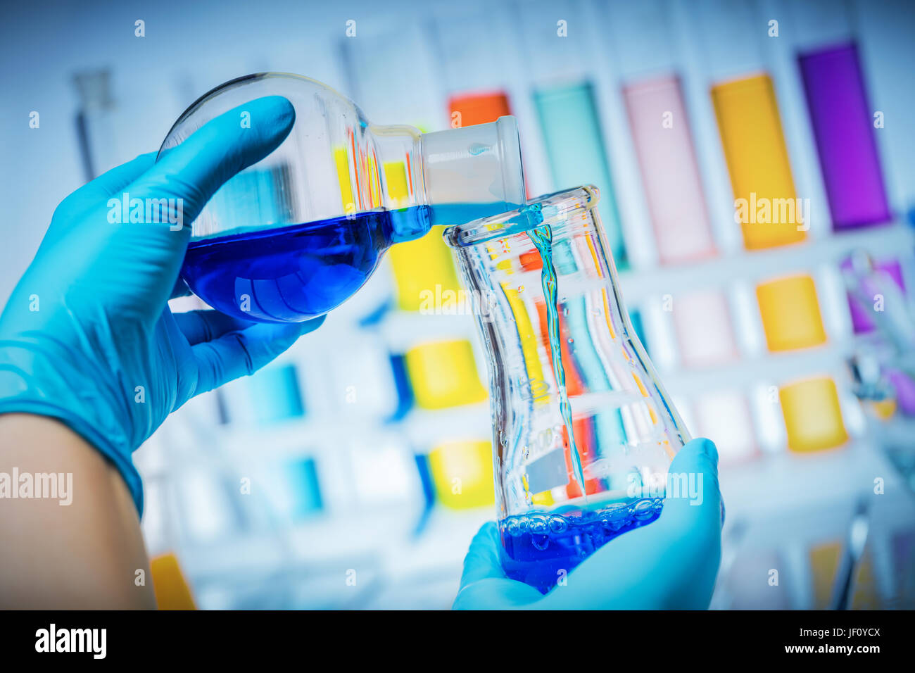 Scientist's hands pouring colorful liquid from tube to a flask ...