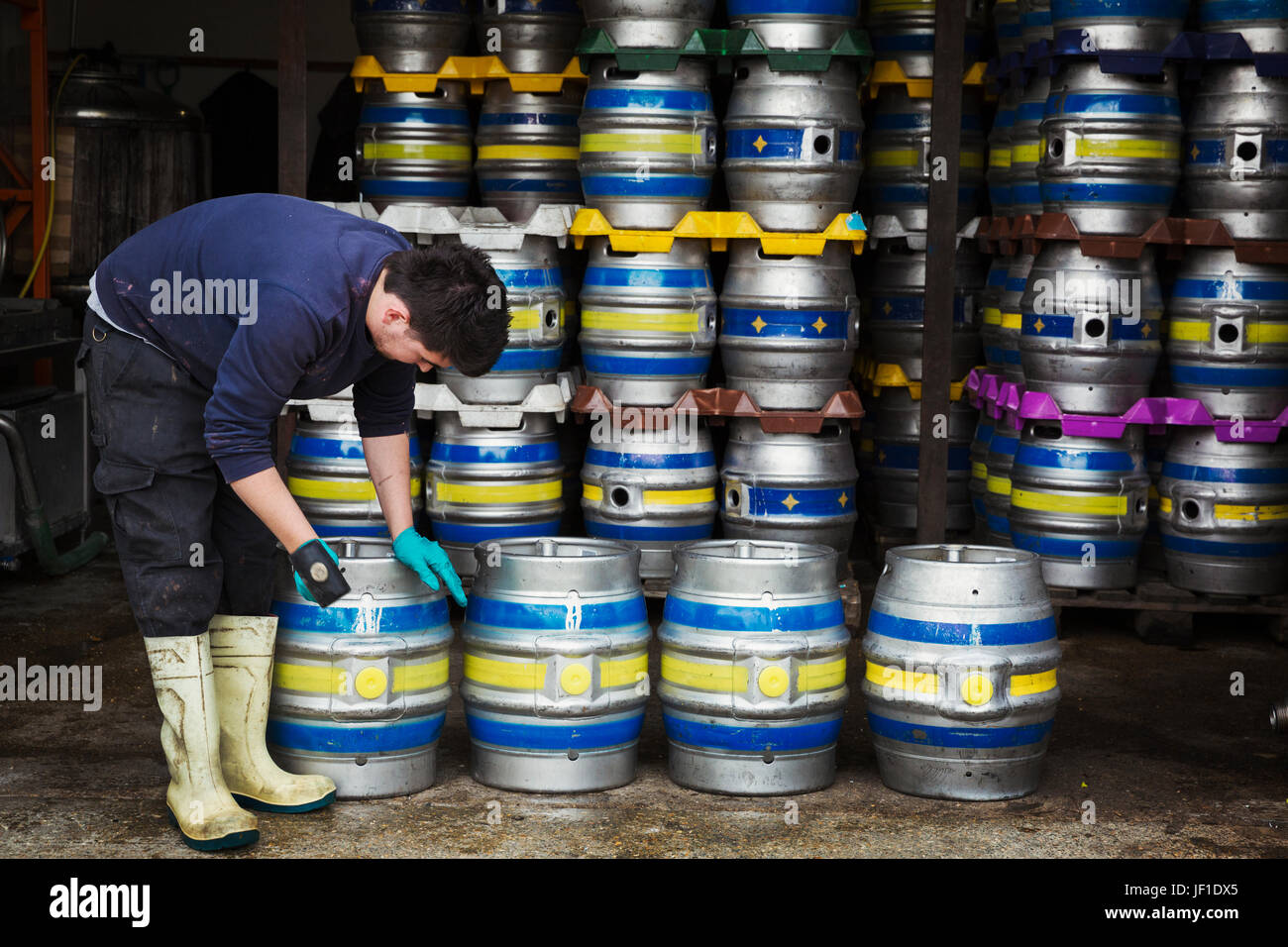 Man working in a brewery, standing next to a stack of metal beer kegs ...