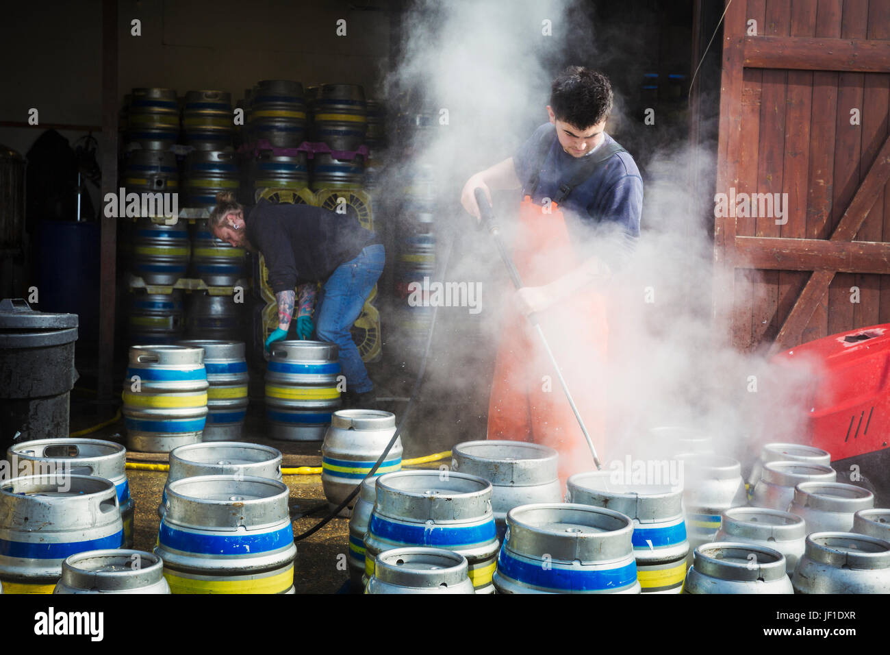 Man working in a brewery, cleaning metal beer kegs with a high pressure ...