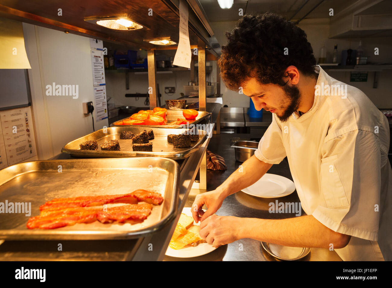 Chef standing in a restaurant kitchen at a counter plating food, trays ...