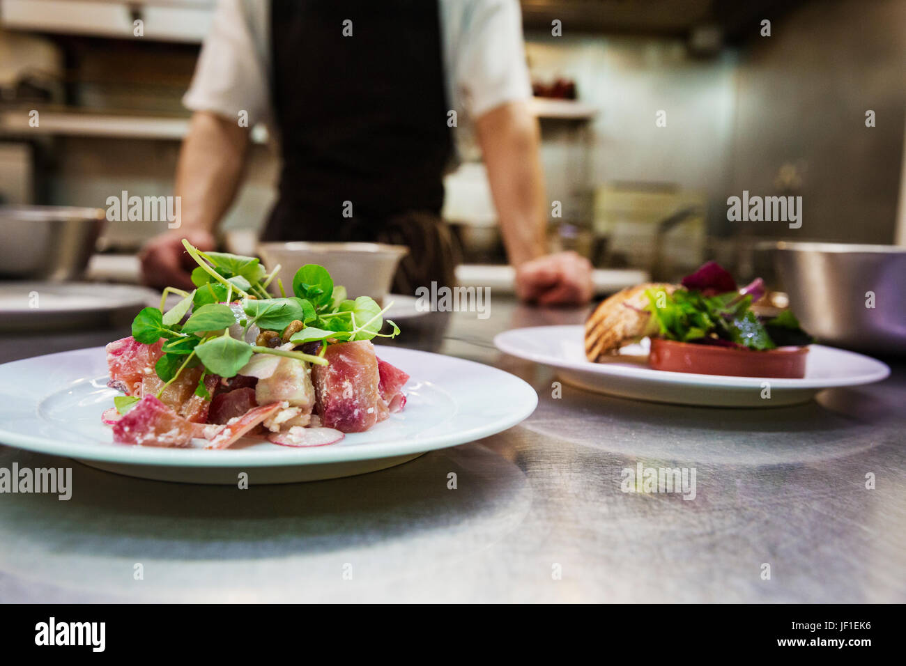 Close up of two plates of food in a kitchen, chef wearing apron ...