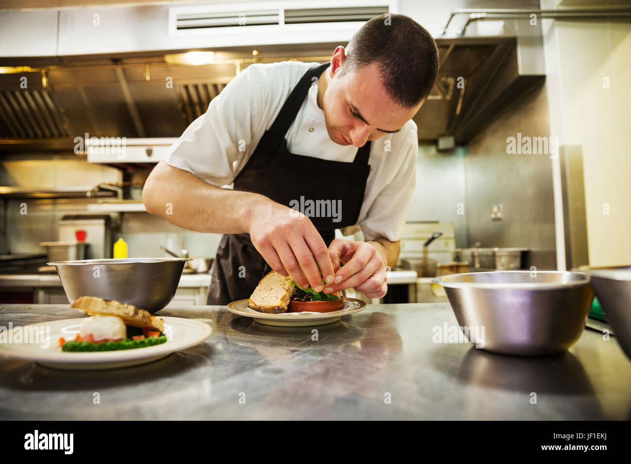 Chef standing in kitchen, wearing apron, plating food Stock Photo - Alamy