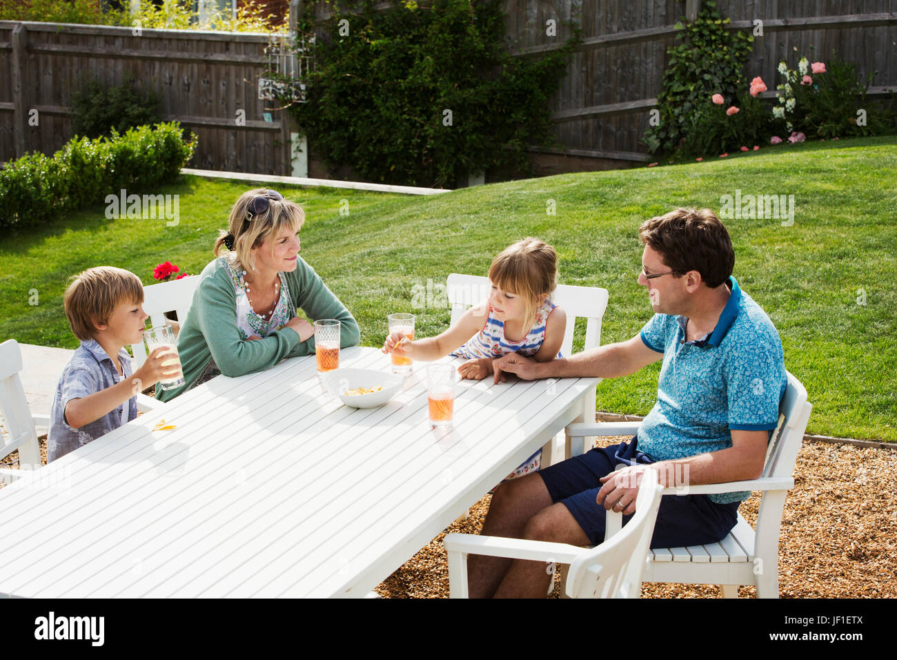 A family sitting around a garden table, parents and two children, a boy ...