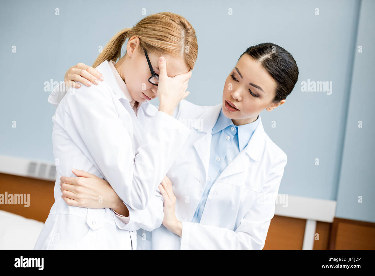 Professional young doctor supporting upset colleague standing in ...