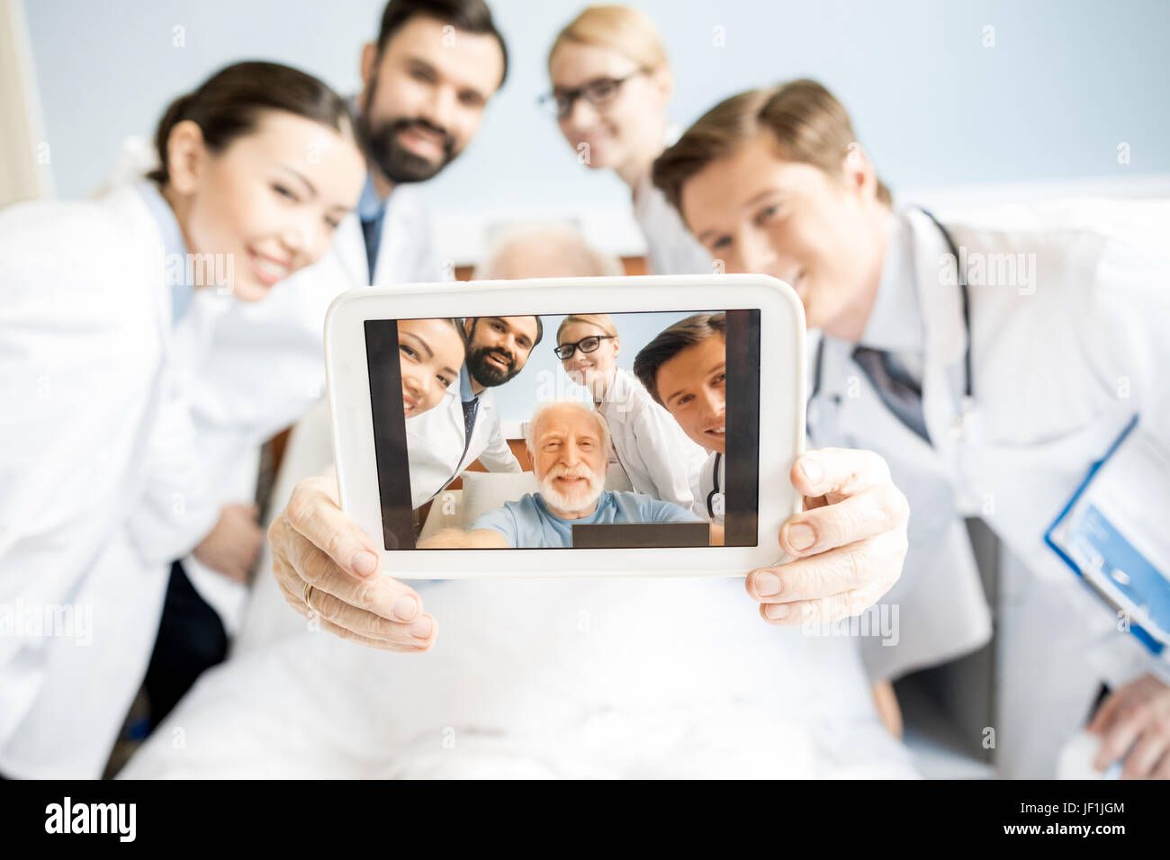 Professional young doctors looking at senior patient using digital ...